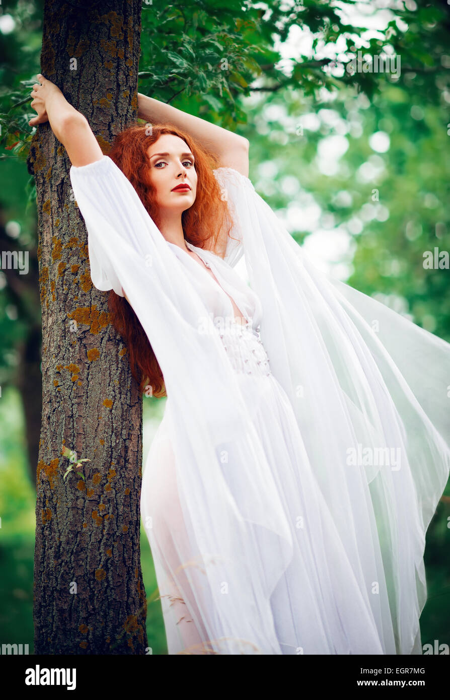 Lovely ginger woman wearing white dress stands near the tree Stock ...