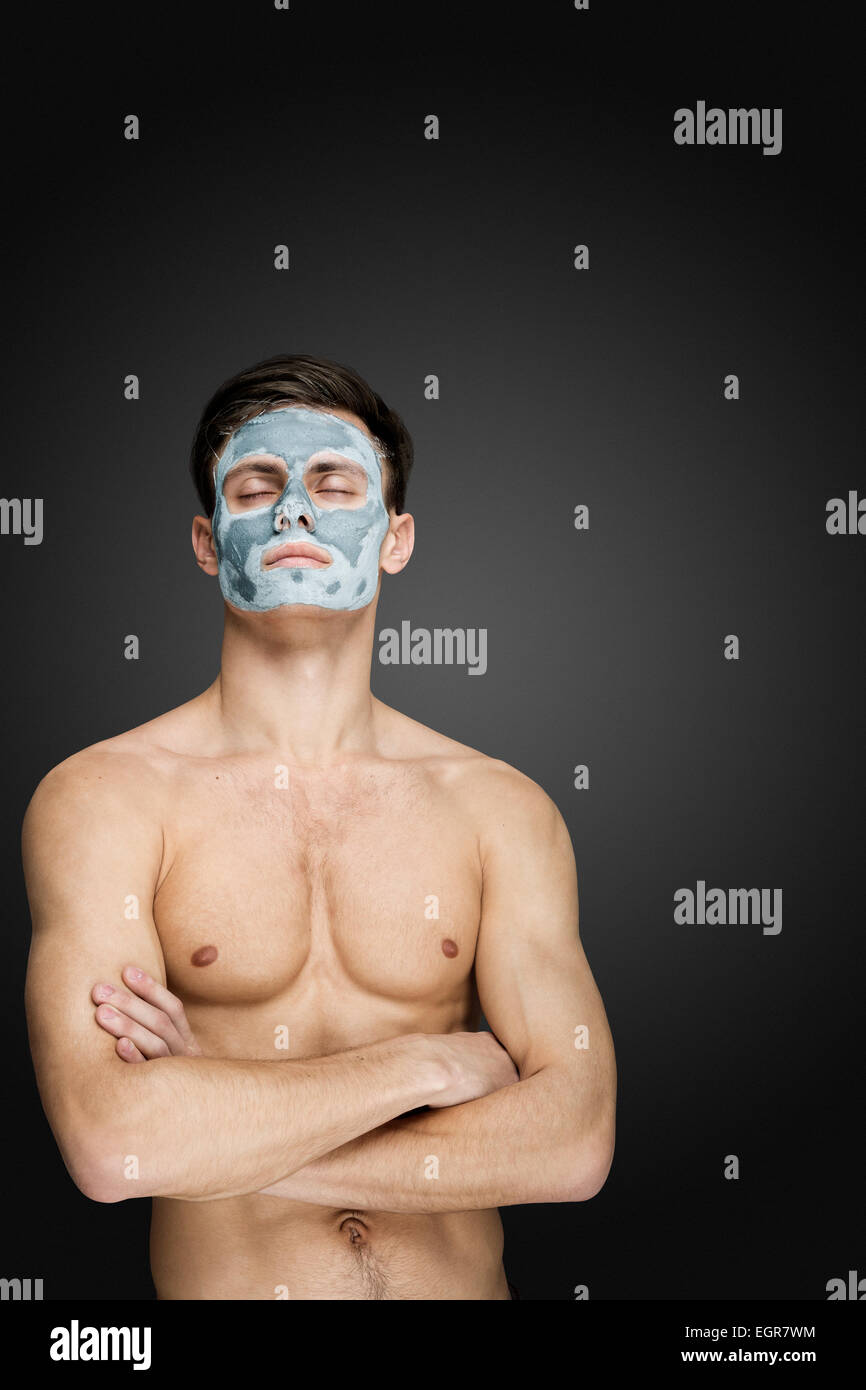 Portrait of a beautiful young man with a facial mud clay mask, face and ...