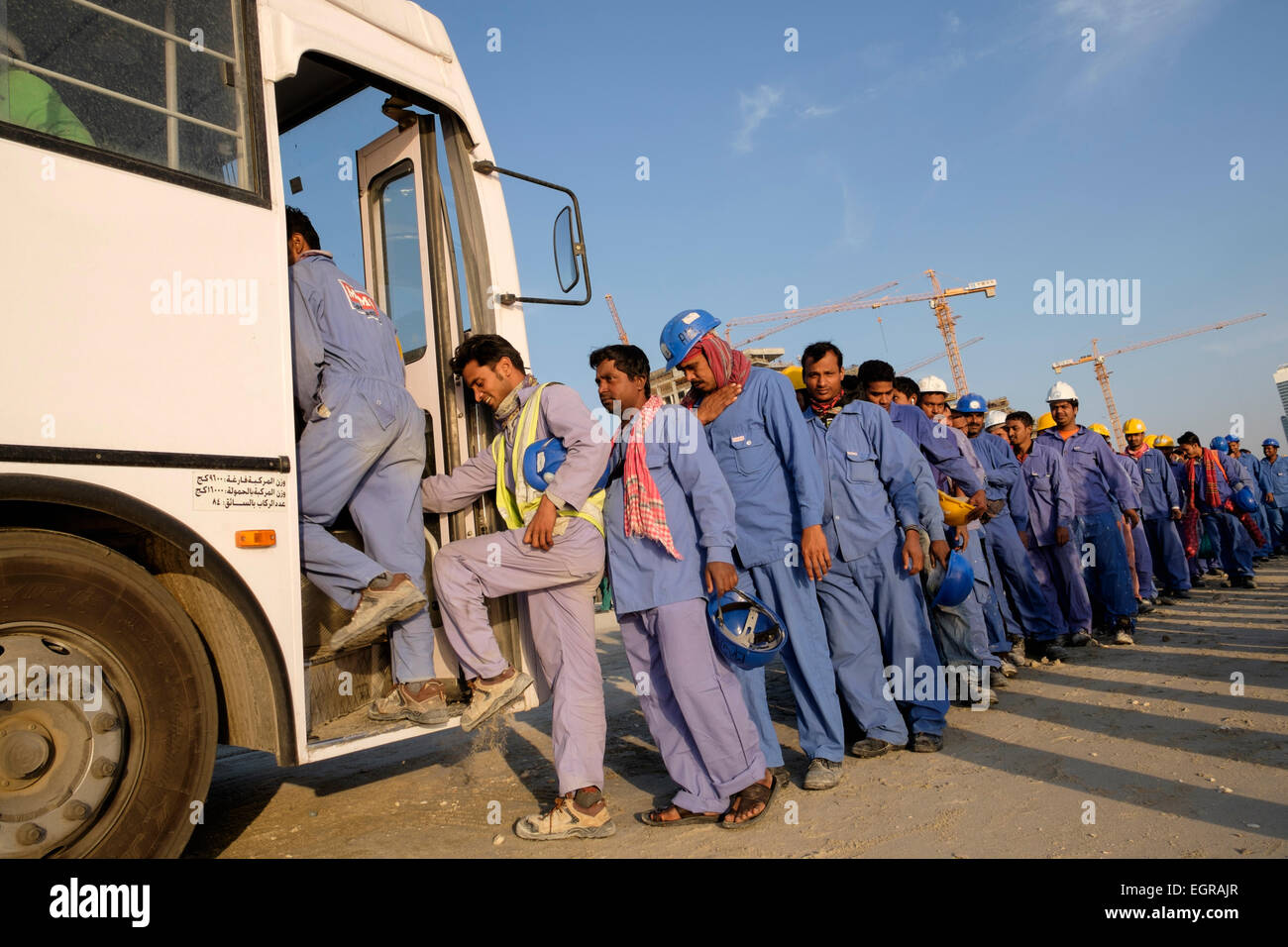 Construction workers queuing to get on bus to living quarters at end ...