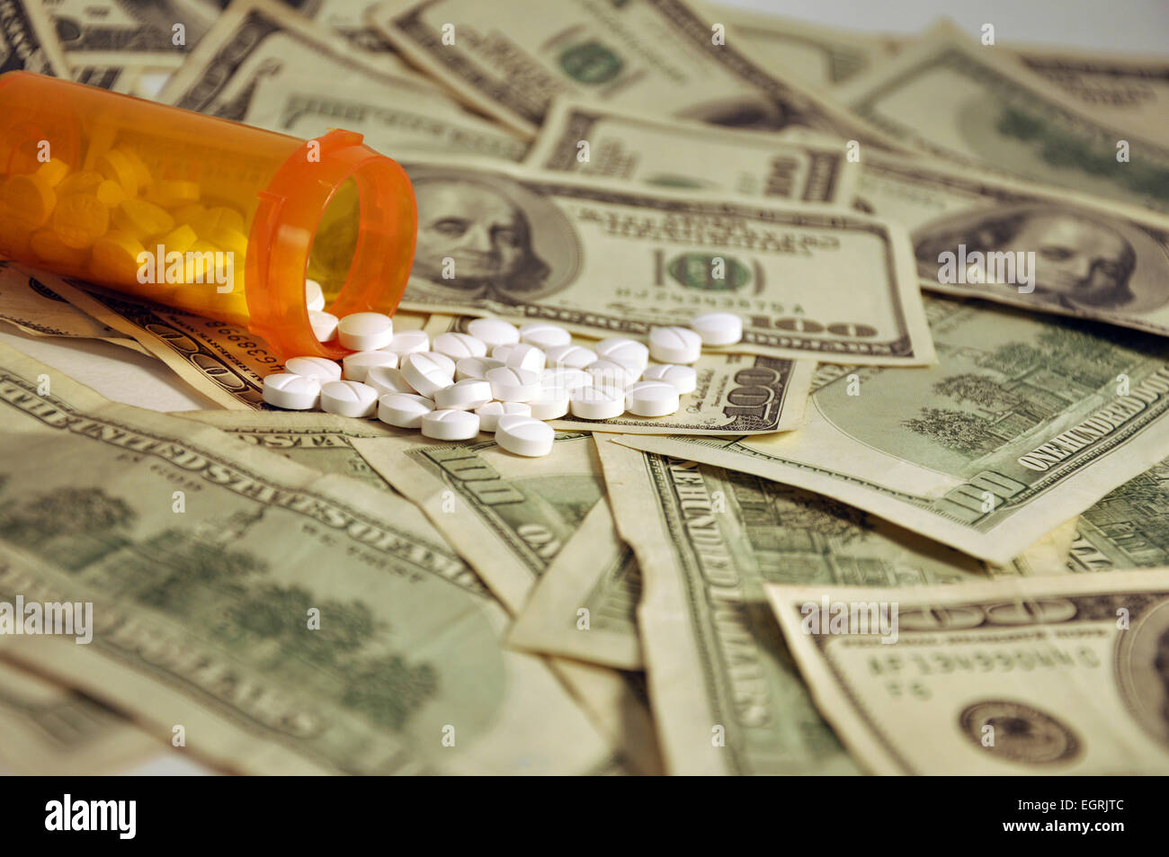 A prescription bottle of white pills spilling on a pile of $100 dollar ...