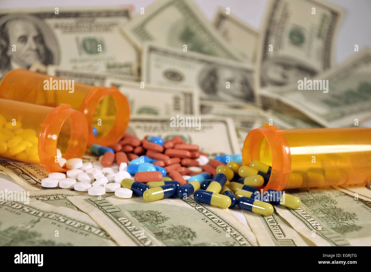 3 bottles of pills spilling over a pile of one hundred dollar bills ...