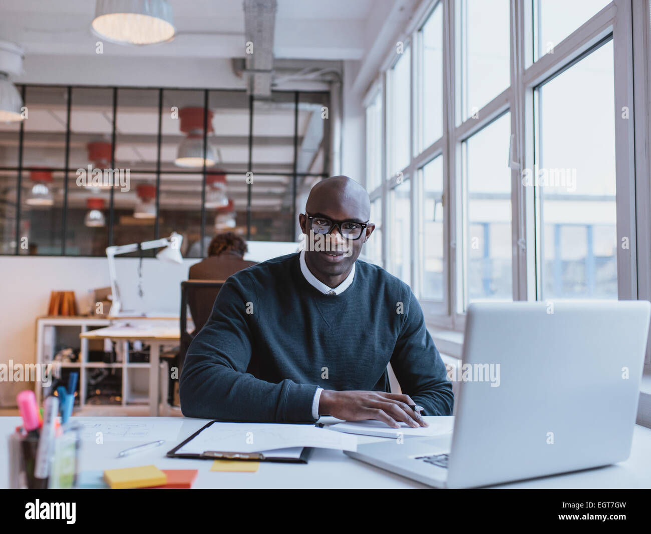 Portrait of confident young man sitting at his desk with laptop ...