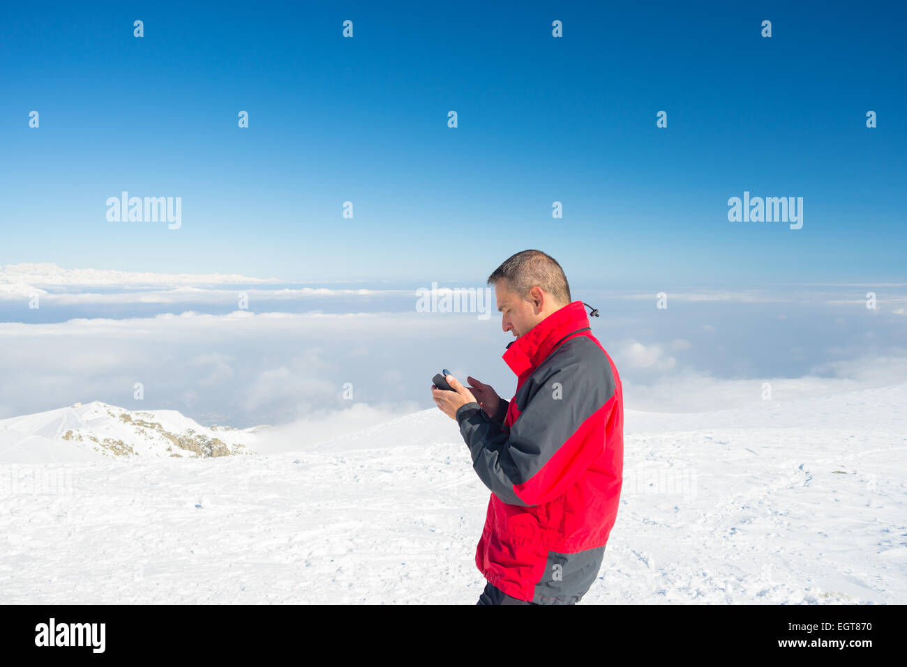 Alpinist with phone in hand on the summit with majestic panoramic view ...