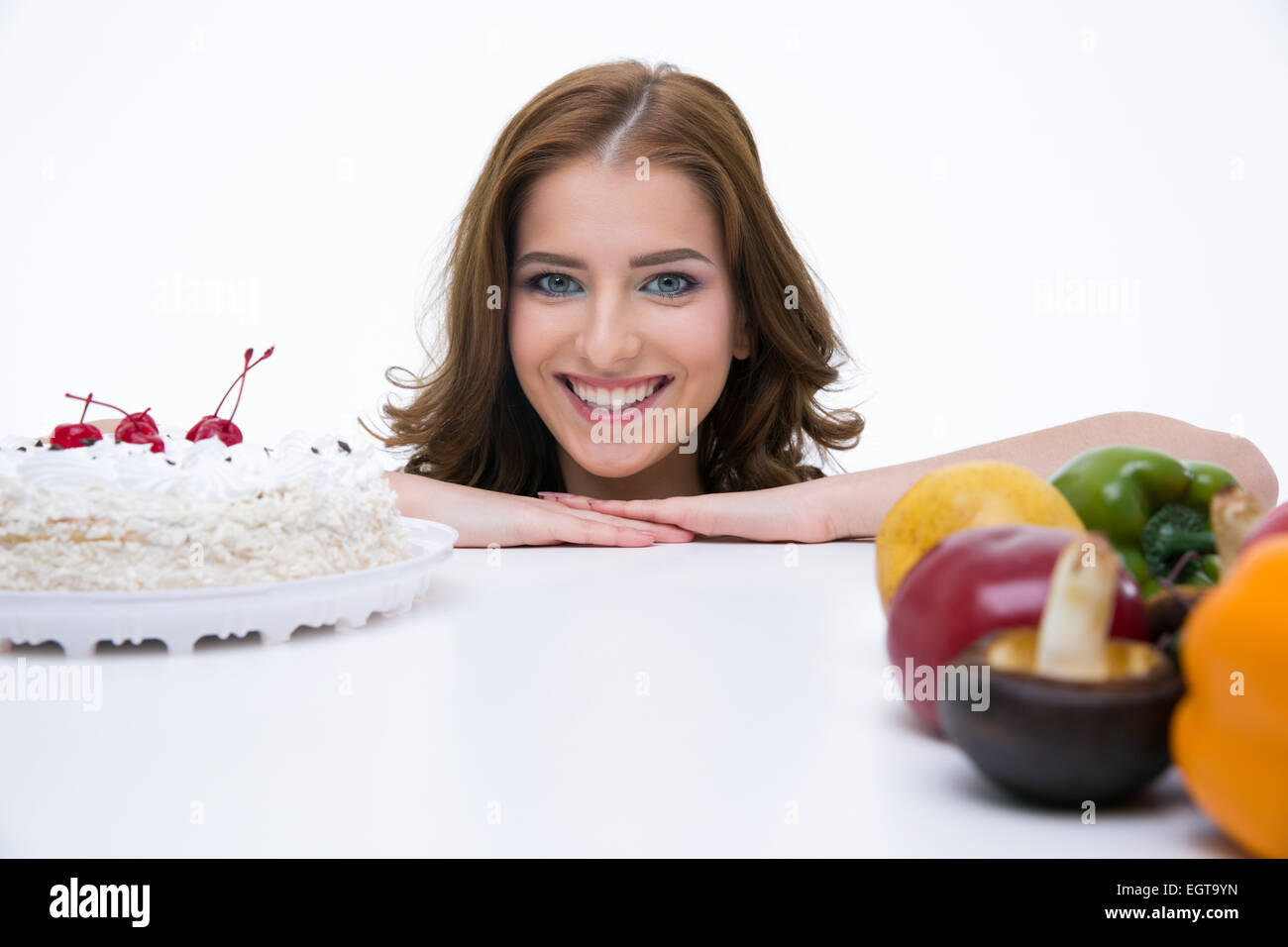 Portrait of a happy woman sitting on the table with cake and vegetables ...