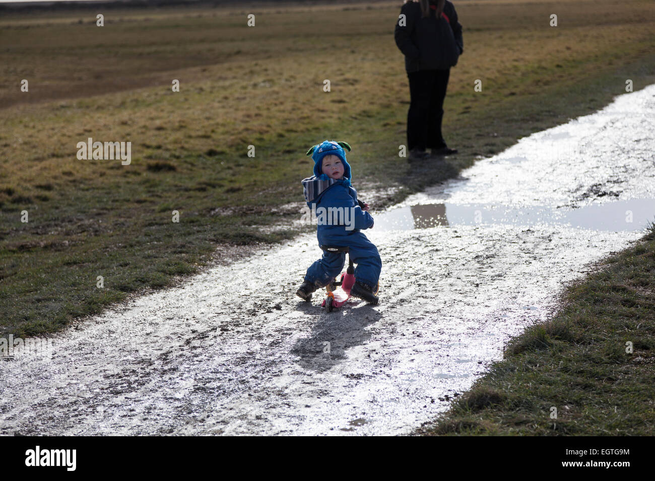 Young child on a scooter on a muddy path on a sunny winter's afternoon ...
