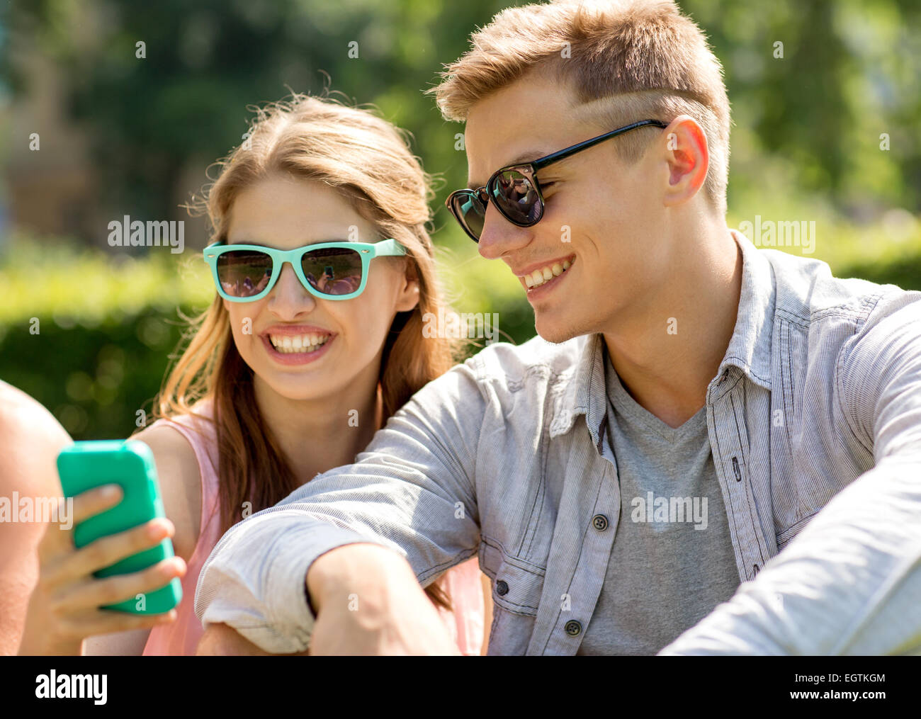 smiling friends with smartphone sitting in park Stock Photo - Alamy