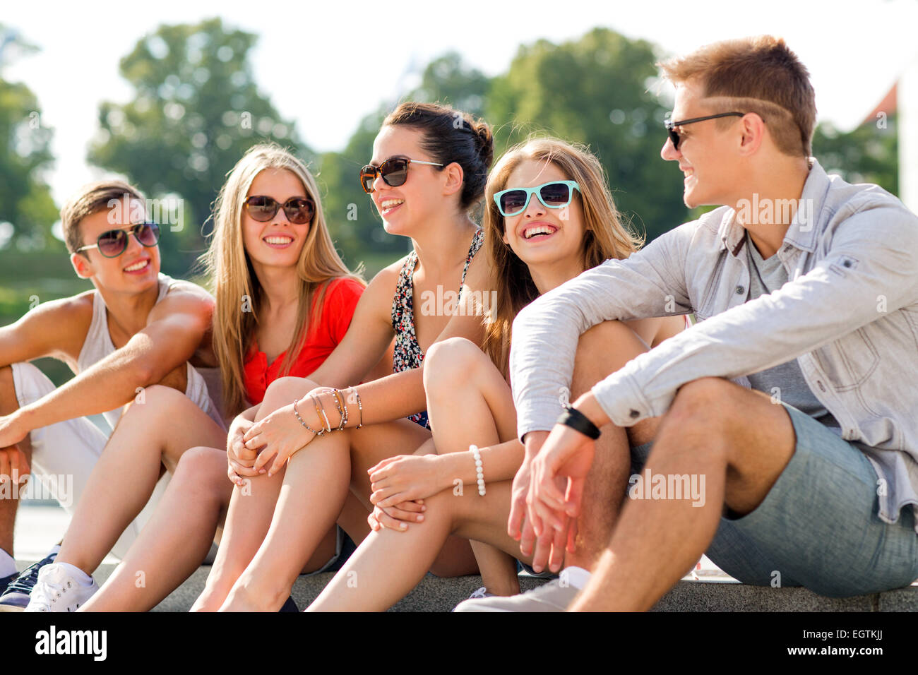 group of smiling friends sitting on city street Stock Photo - Alamy
