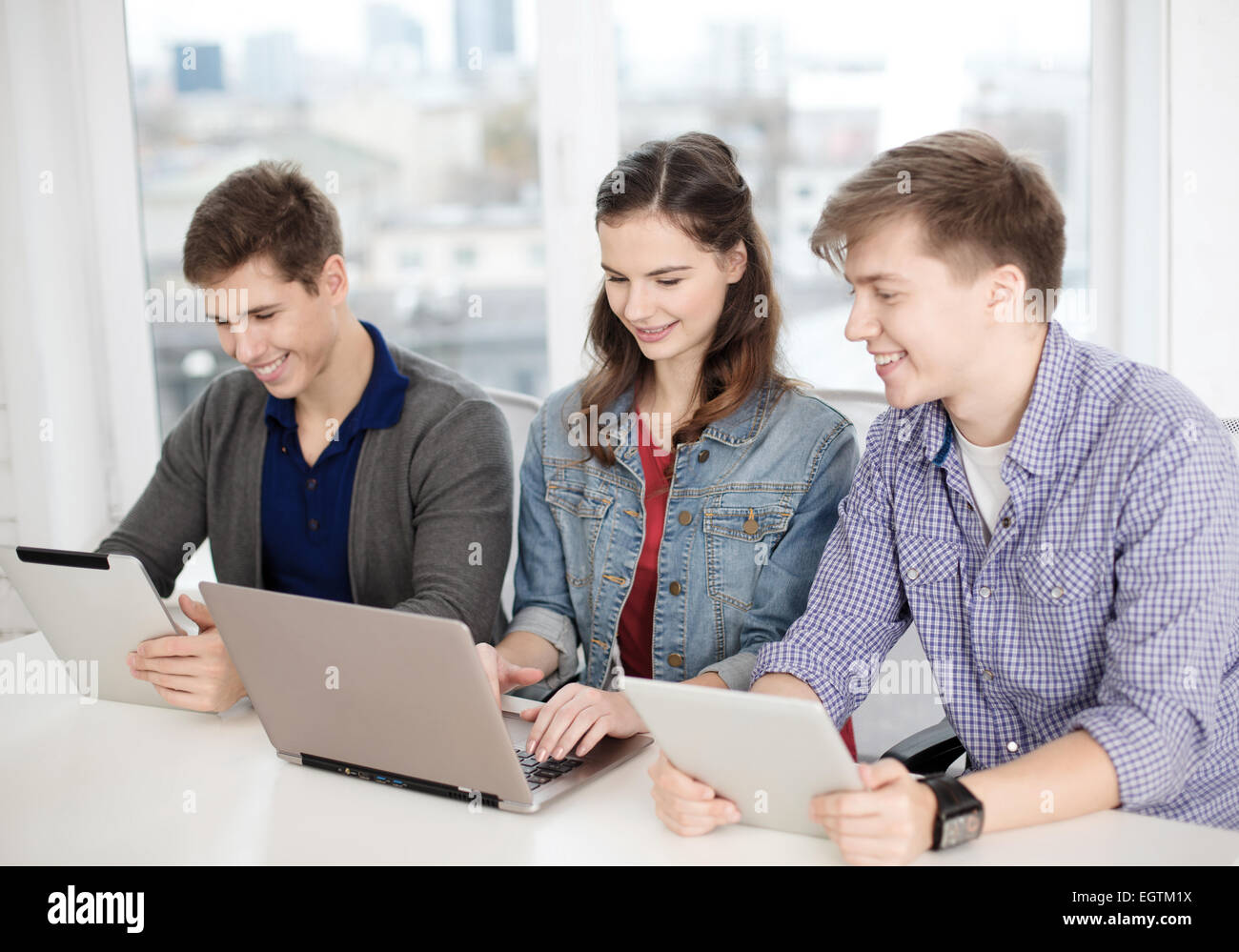 three smiling students with laptop and tablet pc Stock Photo - Alamy