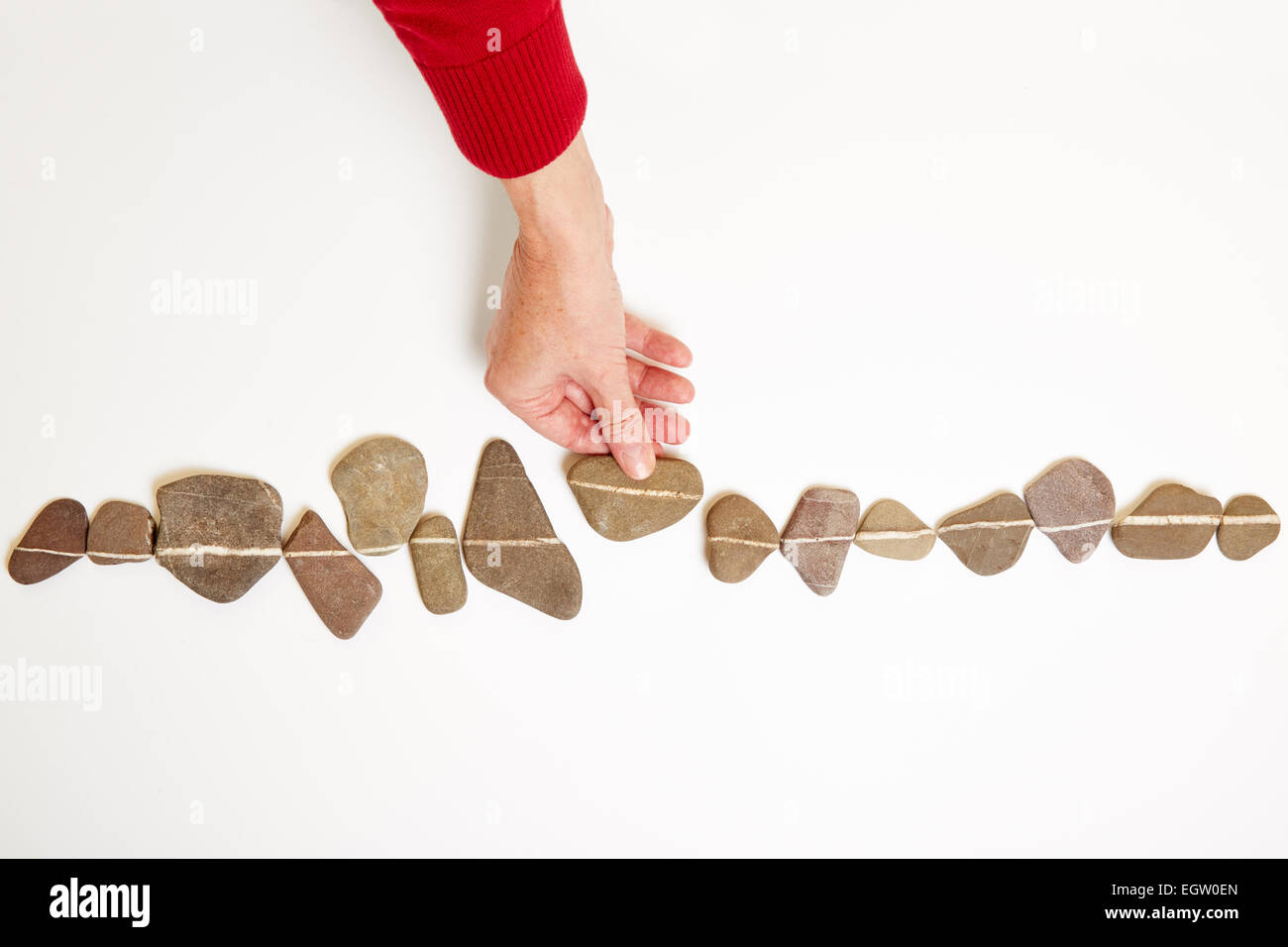 Hand moving stone in line with many other pebbles Stock Photo - Alamy