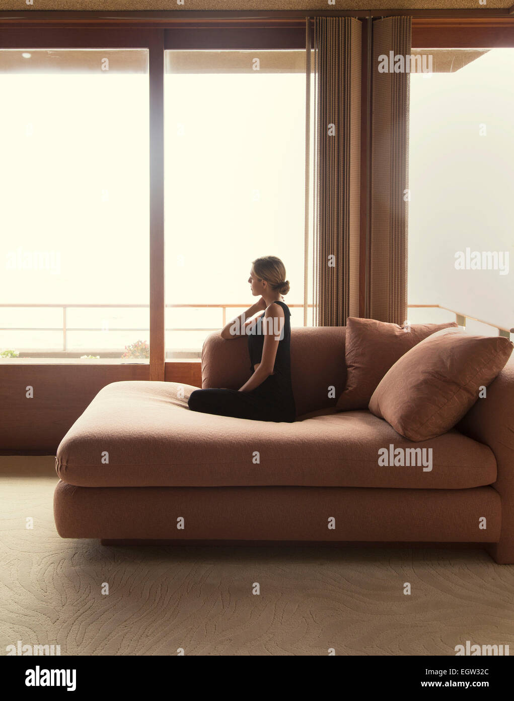 Woman kneeling on sofa, looking out the window Stock Photo - Alamy