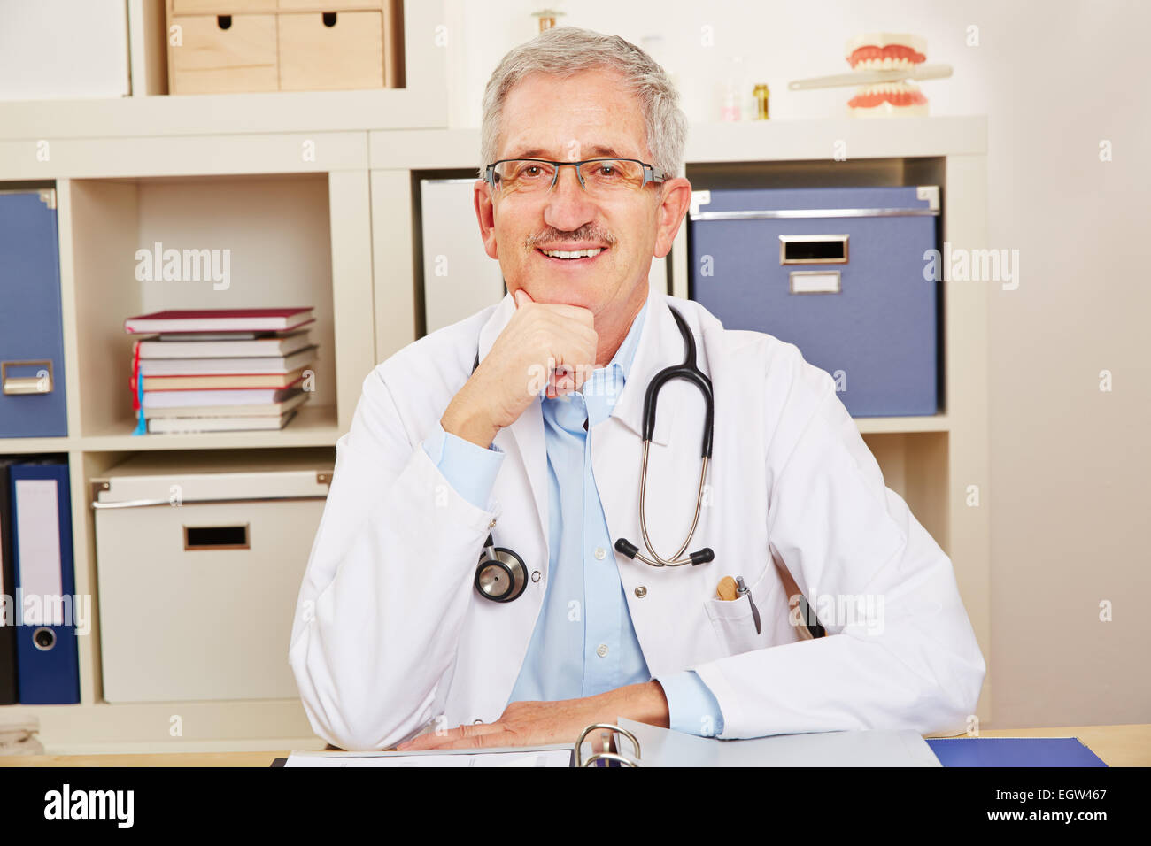 Old doctor sitting smiling at his desk in the office Stock Photo - Alamy