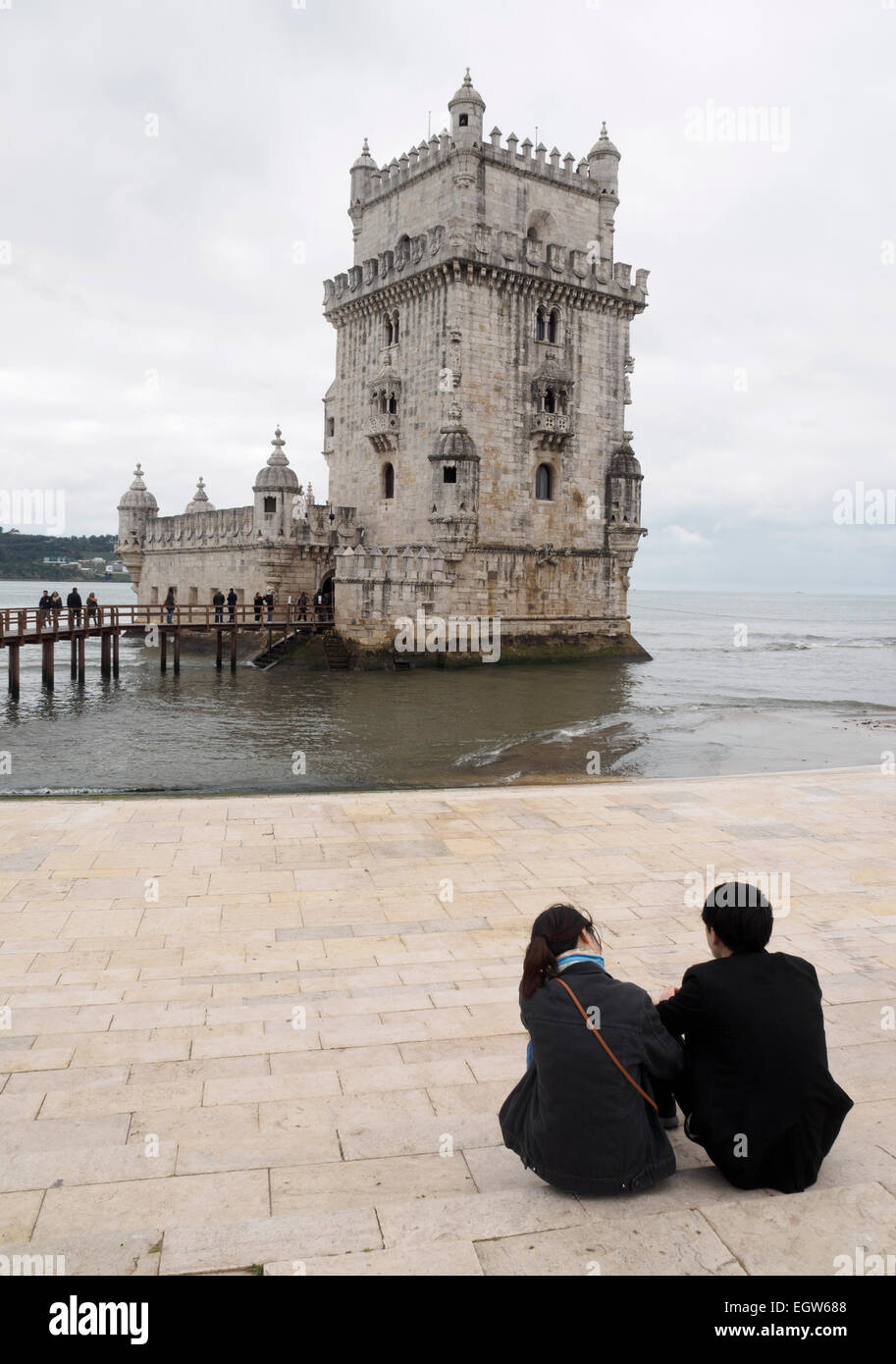 A couple sitting in front of the Belem Tower or Torre de Belém in ...