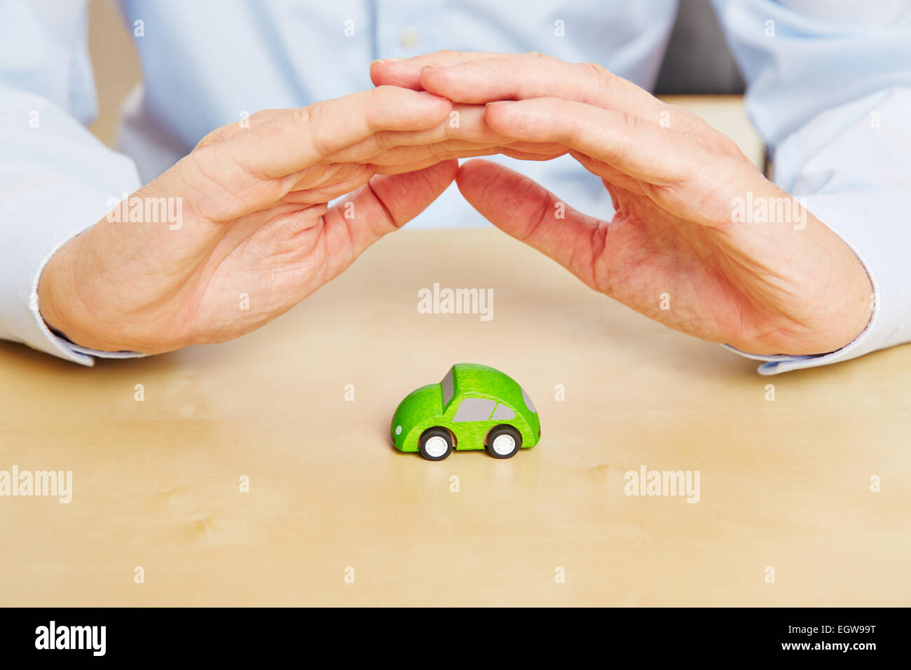 Two hands protecting a small green car as concept for car insurance ...