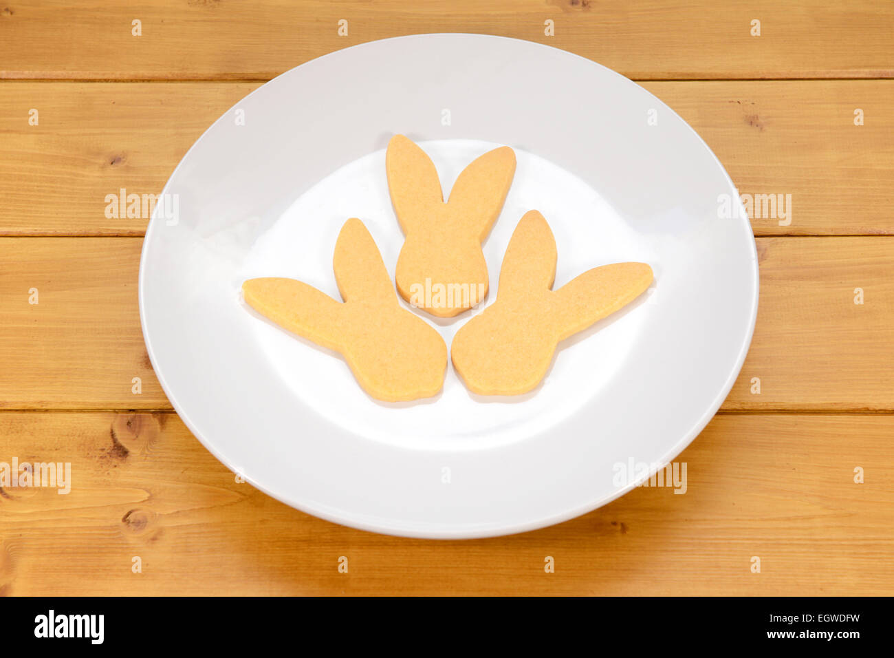 Three rabbit-shaped biscuits for Easter on a white plate on a wooden ...