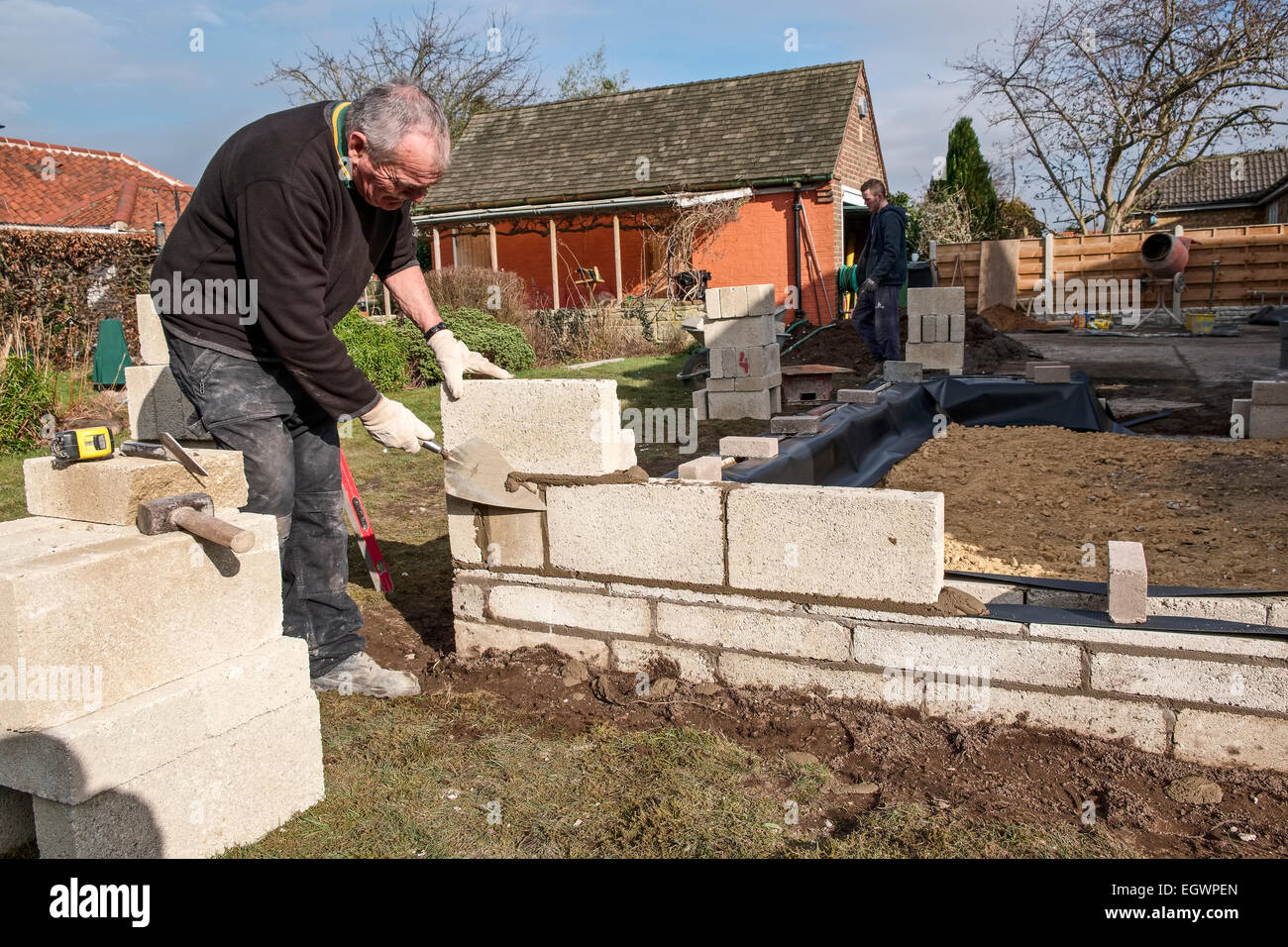 Bricklayer trimming excess mortar cement whilst building a breezeblock ...