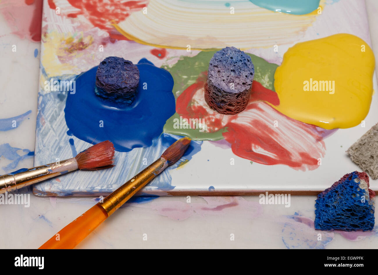Artists paintbrush paints and sponge on a tile used as a paint palette ...
