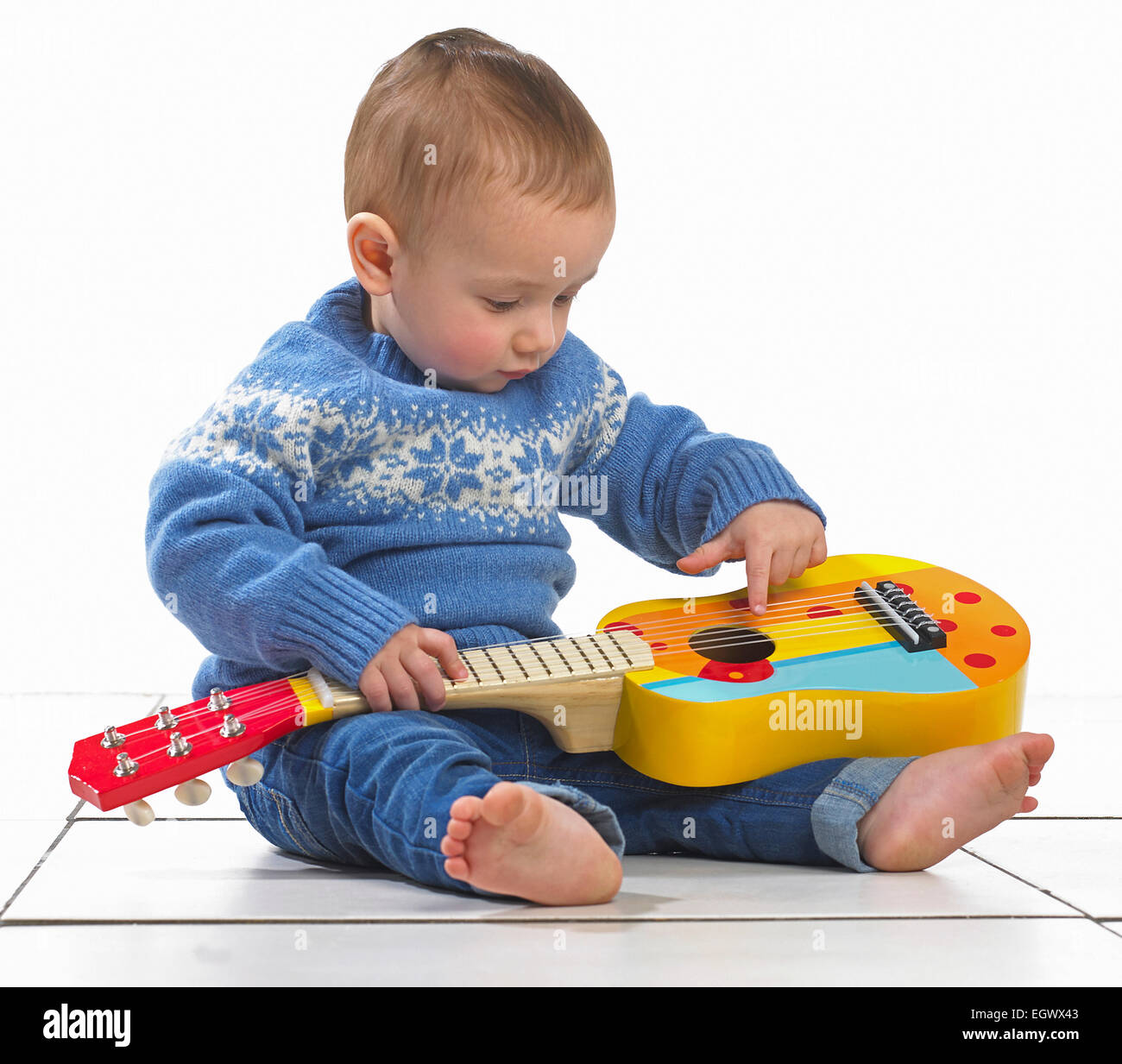 Baby boy (12.5 months) sitting playing with toy guitar Stock Photo - Alamy