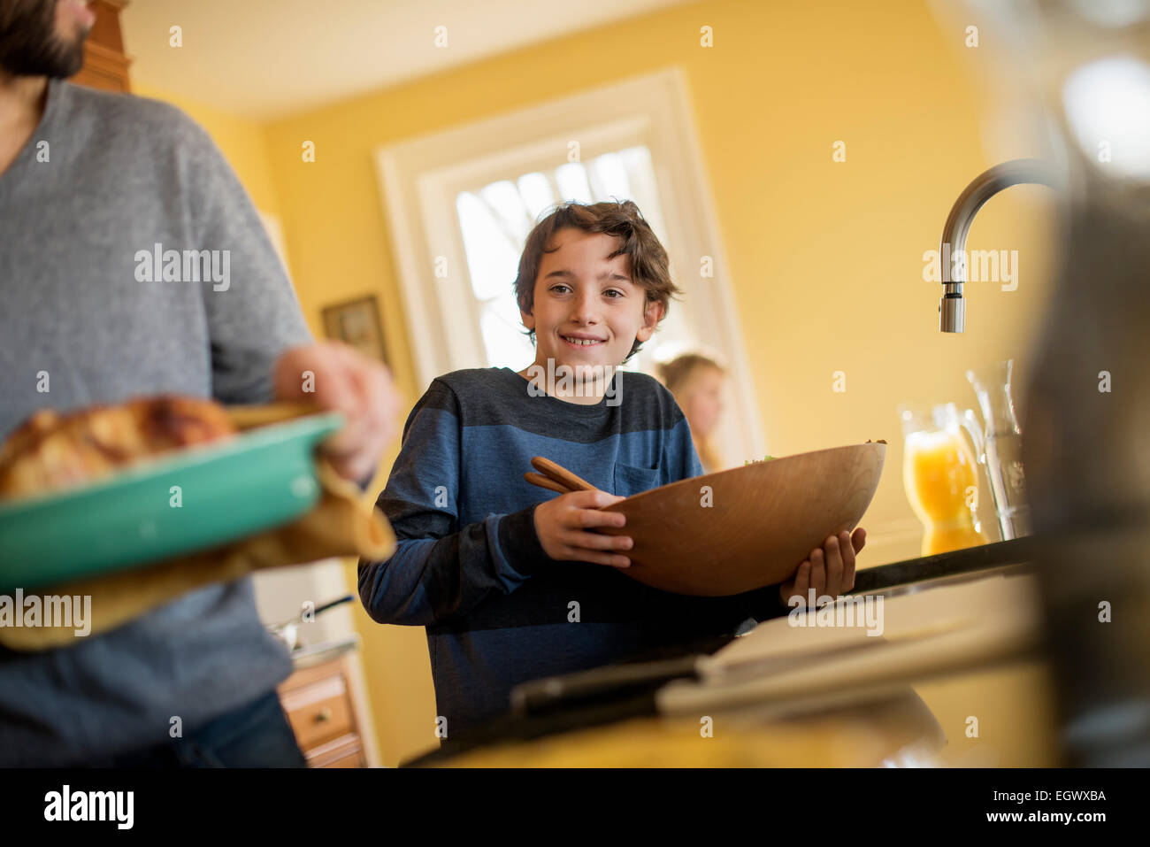 A woman carrying prepared food to the table. A boy with a large wooden ...