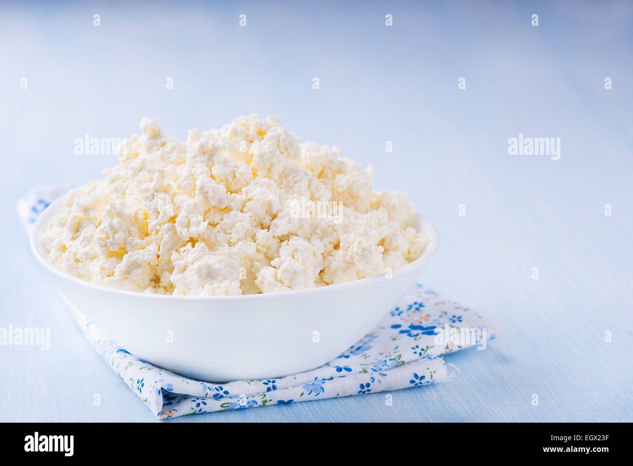 Cottage cheese in white bowl over light blue background, selective ...