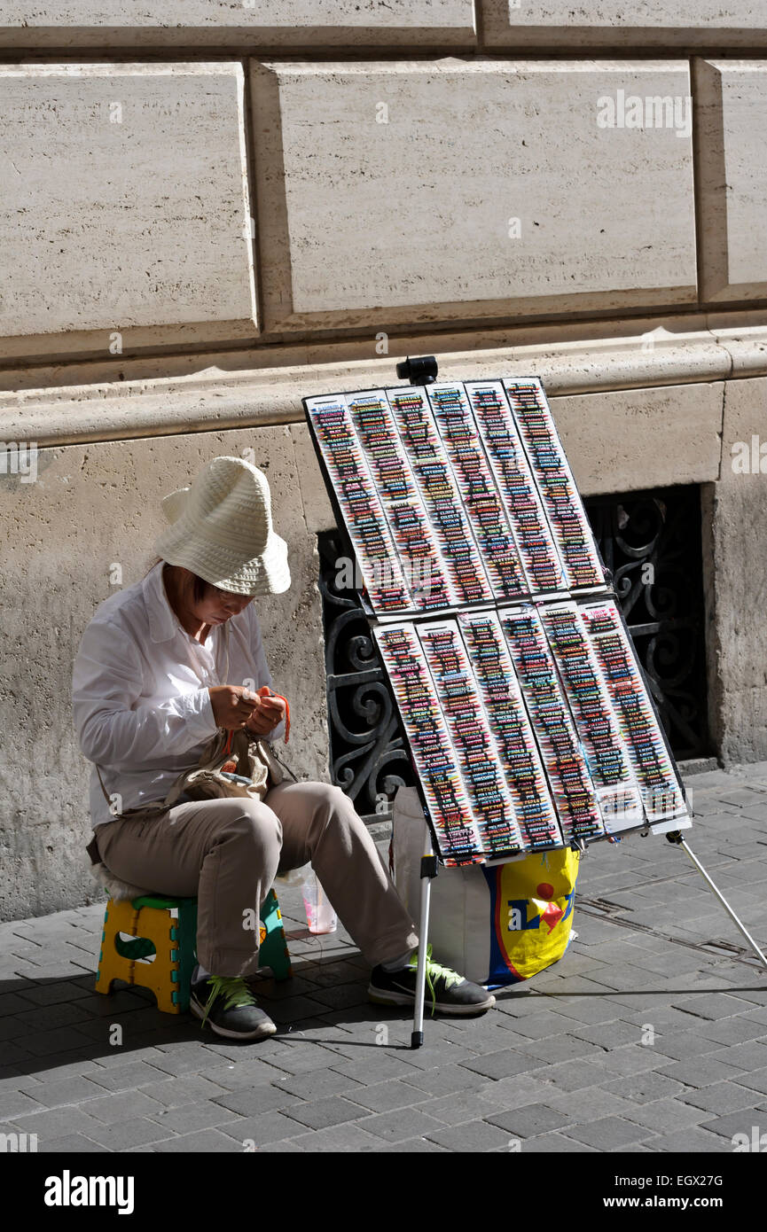 A street vendor sitting on a small stool by a board with handmade names ...