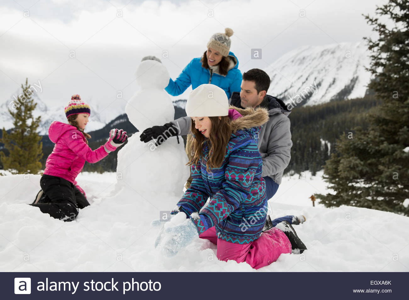 Family making snowman below mountains Stock Photo - Alamy