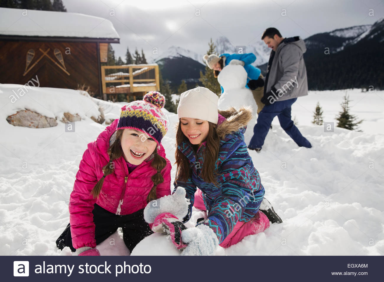 Family making snowman below mountains Stock Photo - Alamy