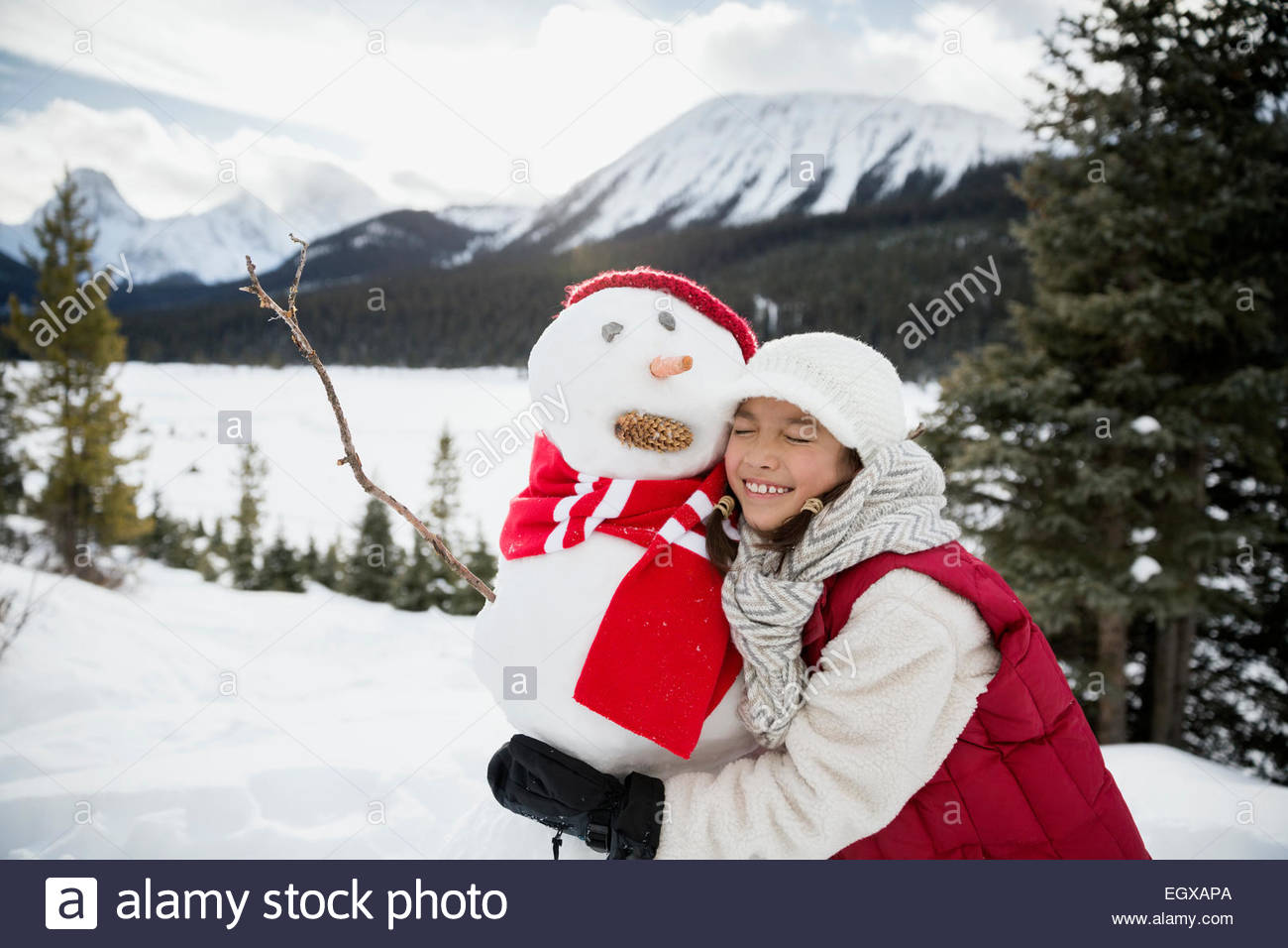 Enthusiastic girl hugging snowman below mountains Stock Photo - Alamy