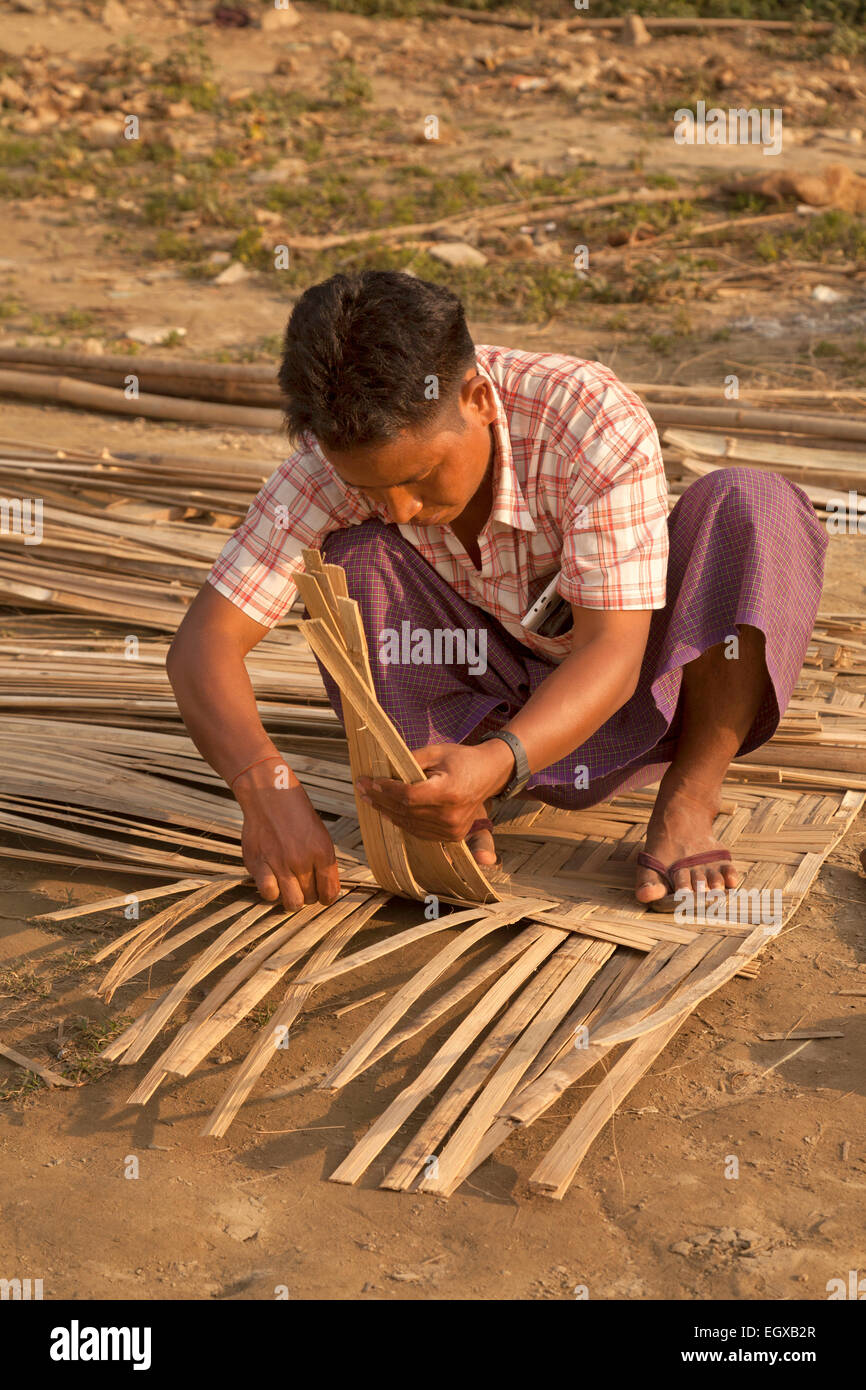 A craftsman weaving the roof of a hut out of wooden slats, Mandalay ...