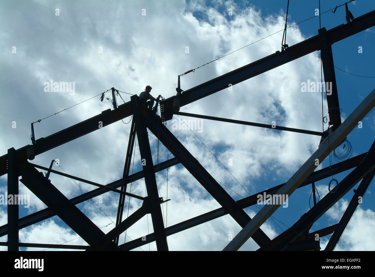 Silhouette of a construction worker guiding steel beam into place as a ...
