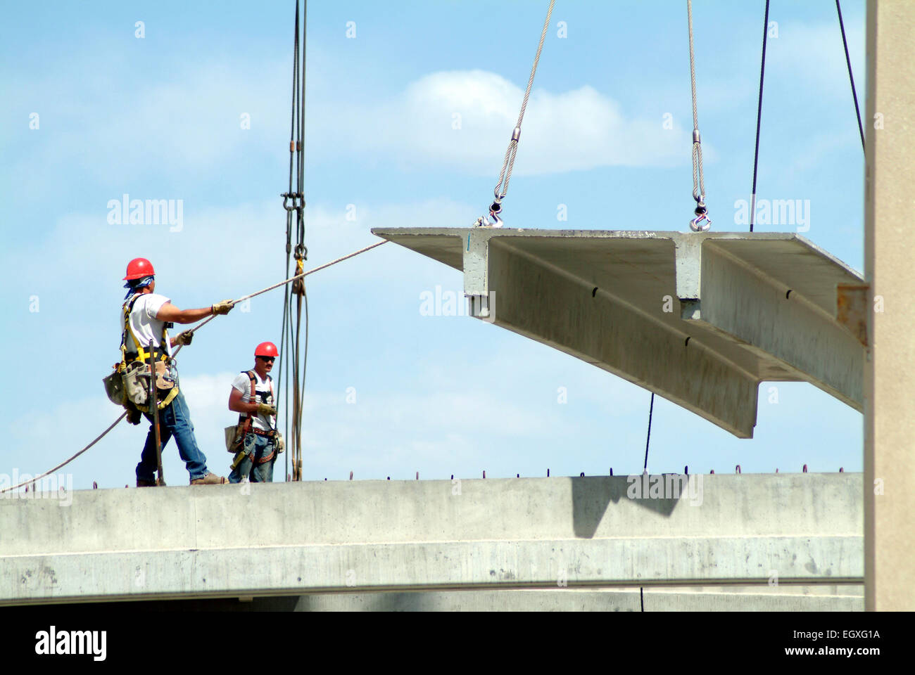 Construction workers guide a structural precast concrete double T beam ...