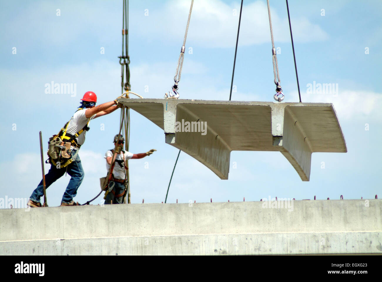 Construction workers guide a structural precast concrete double T beam ...