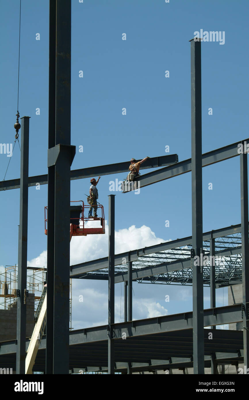 Construction workers guide a steel beam into place as a crane lowers it ...