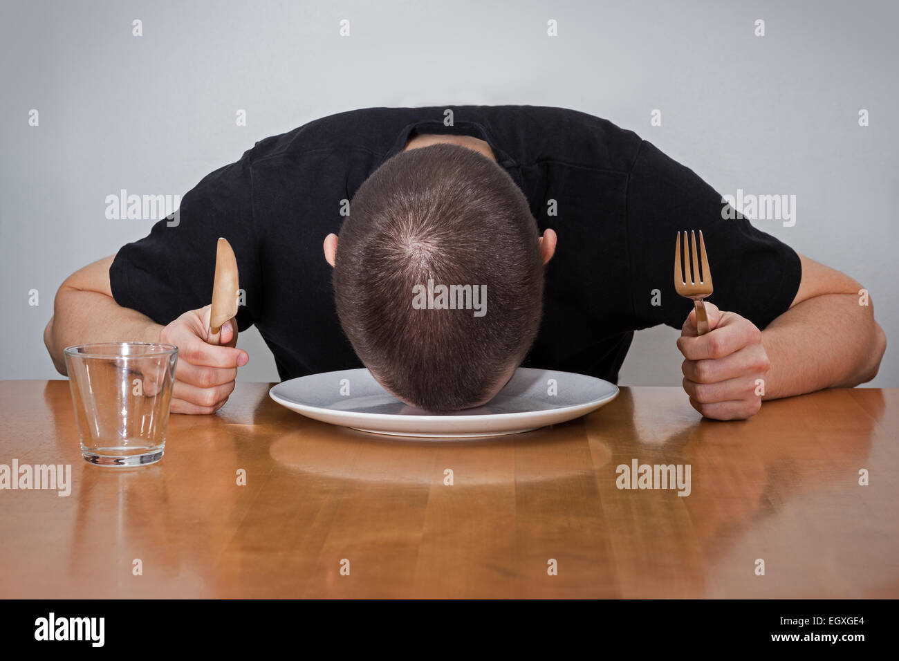 An unrecognizable man holding fork & knife, sleeping head on a plate on ...