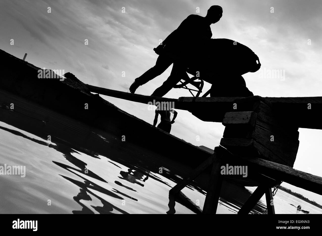 Colombian sand miners, using a wheelbarrow, unload sand from the boat ...