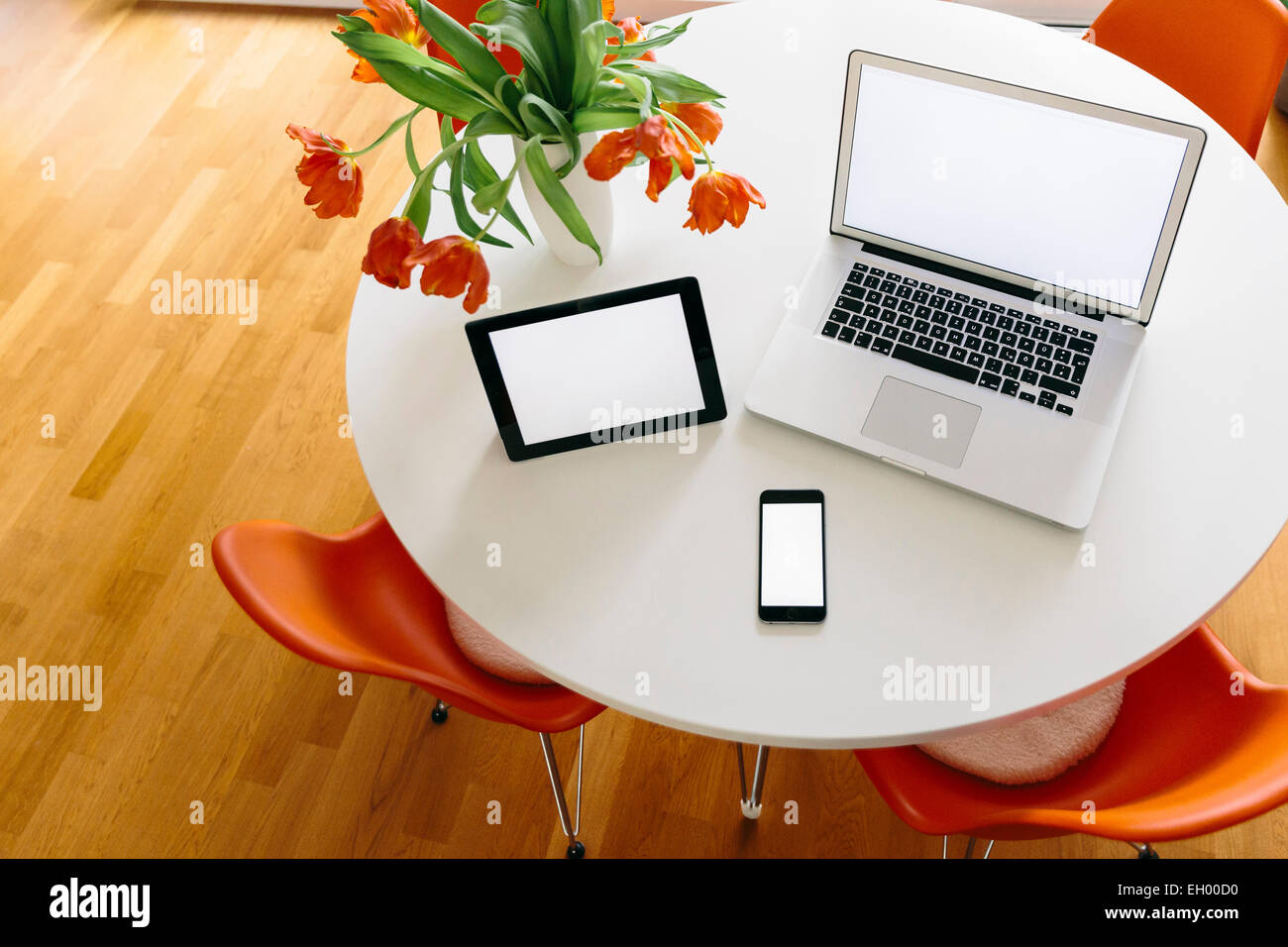 Three mobile devices on a white round table with red tulips and chairs ...