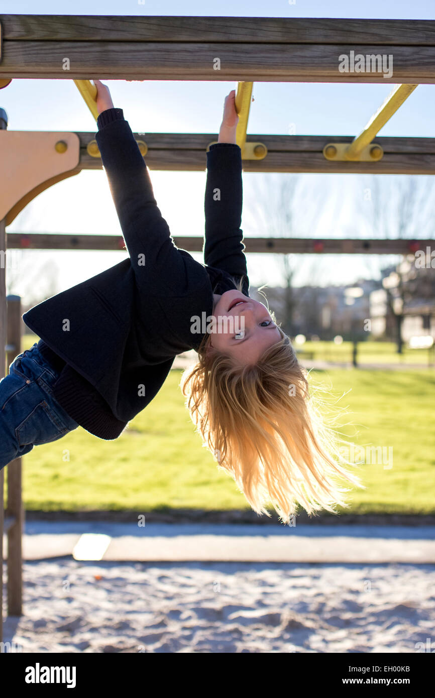 Girl hanging head first on playground equipment Stock Photo - Alamy