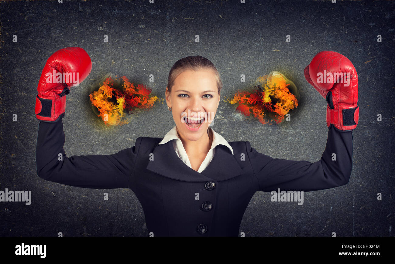 Confident woman in red gloves with fire from ears. Concrete gray wall ...