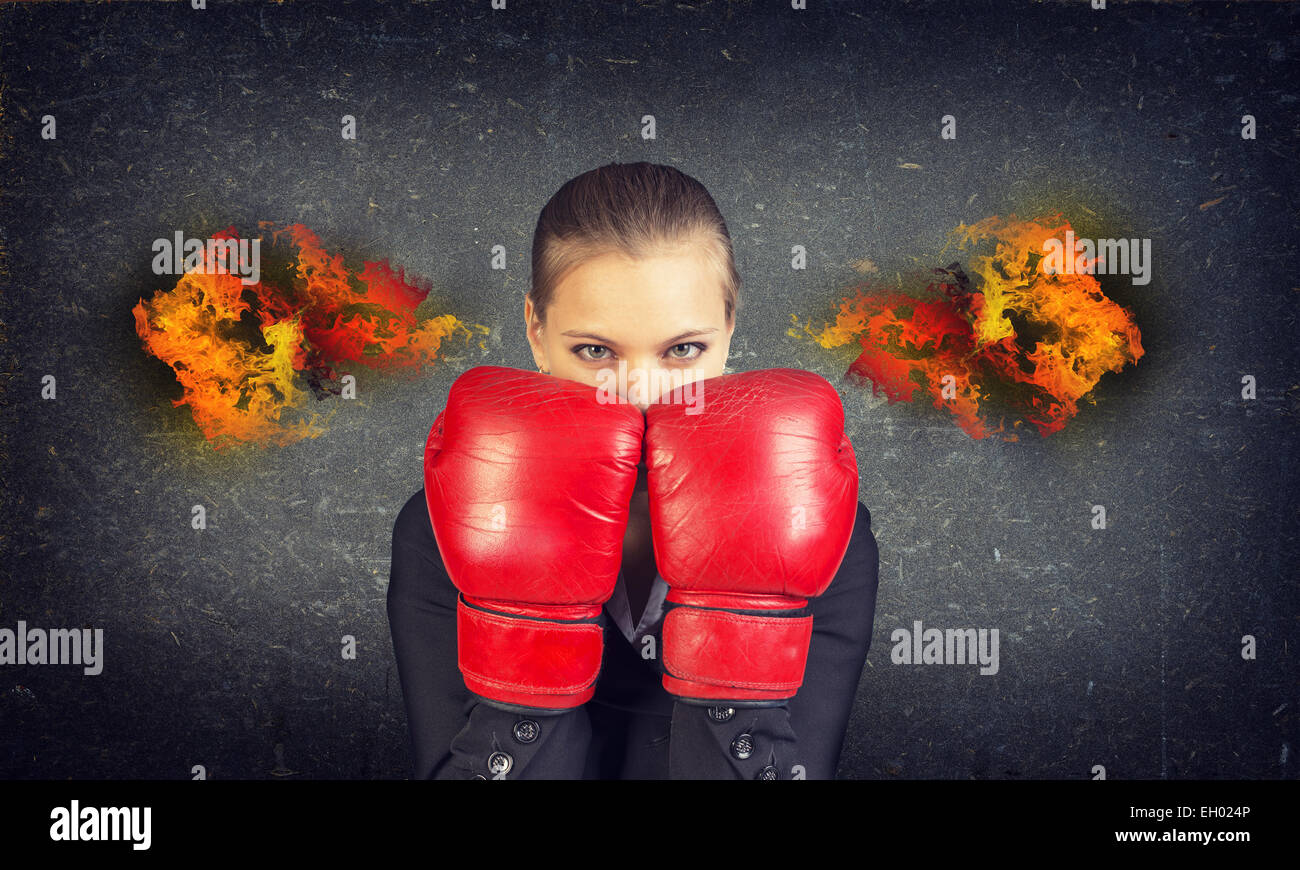 Woman boxing gloves covers her face. Fire from ears. Concrete gray wall ...