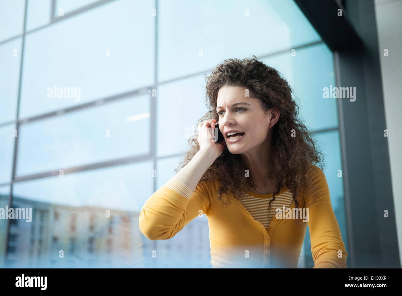 Angry young woman on the phone at the window Stock Photo - Alamy
