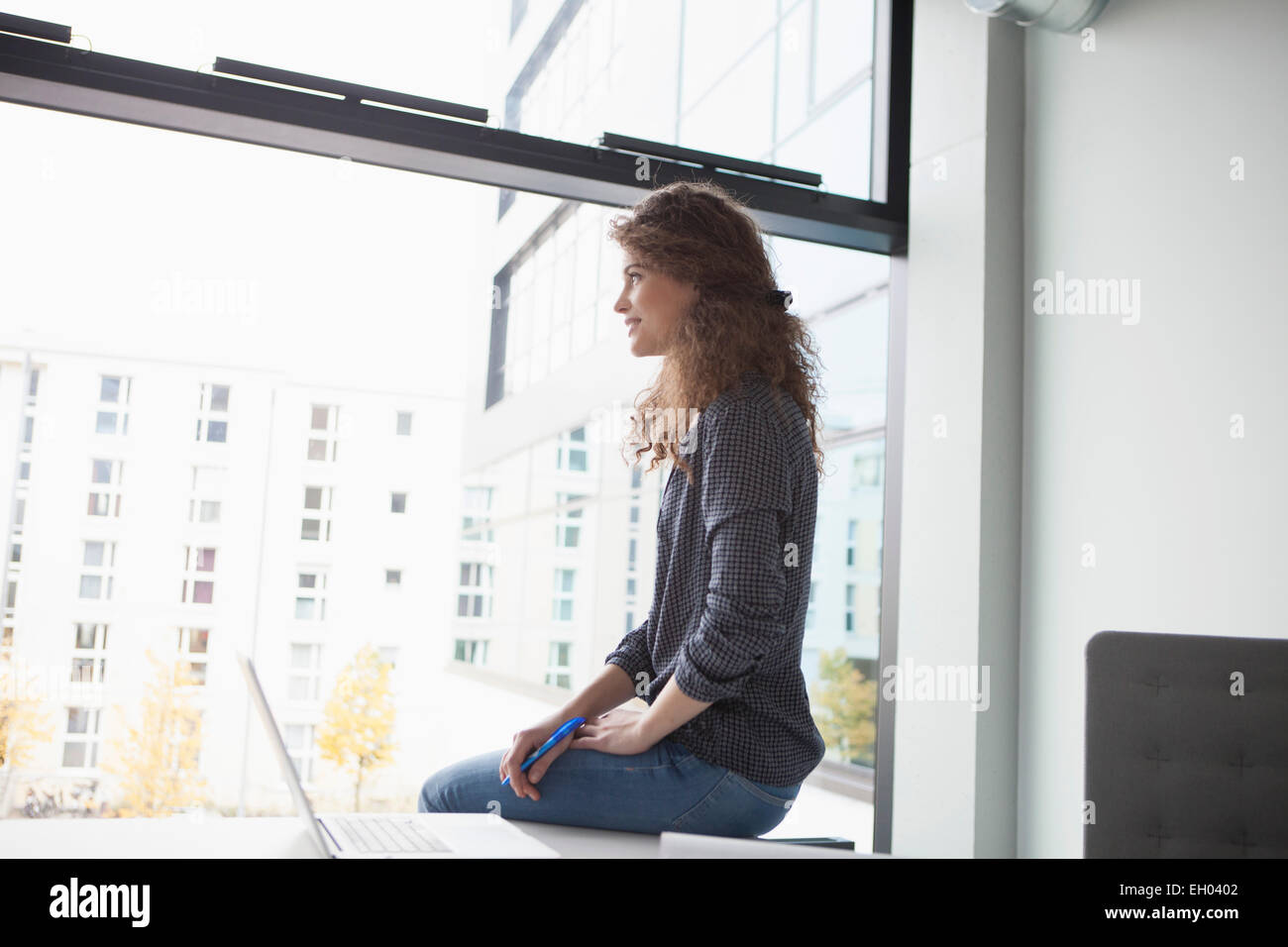 Young woman at desk in office looking out of window Stock Photo - Alamy