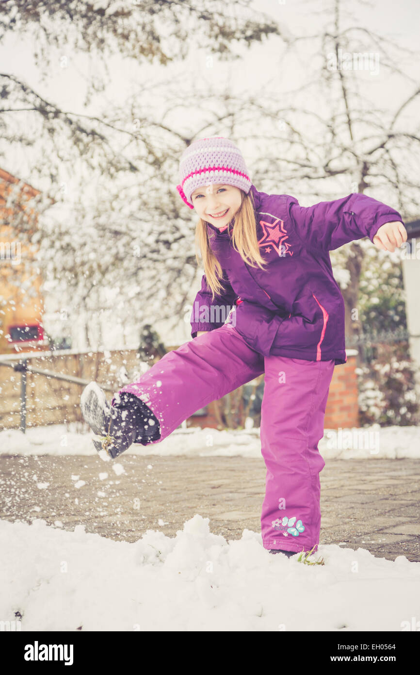 Smiling little girl kicking snow Stock Photo - Alamy