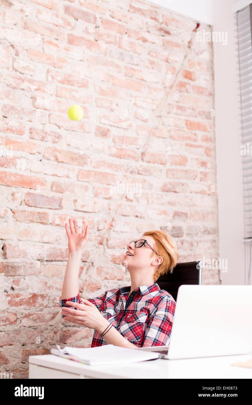 Young woman throwing tennis balll at desk Stock Photo - Alamy
