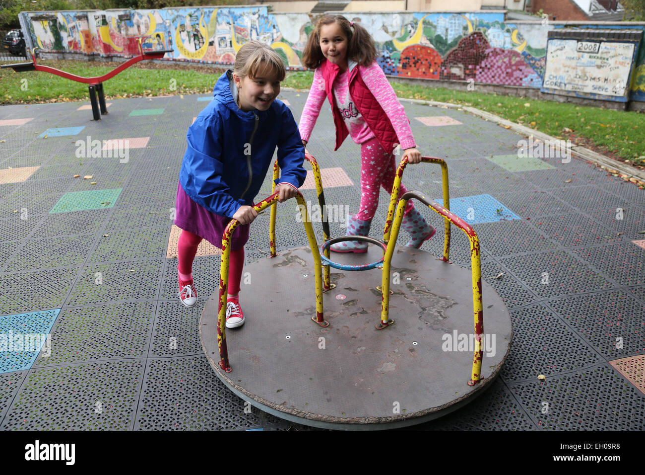 Two girls on roundabout in urban park - model released Stock Photo - Alamy