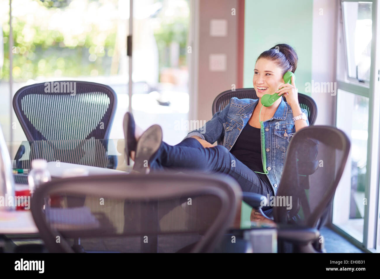 Female creative professional telephoning with feet up in the office ...