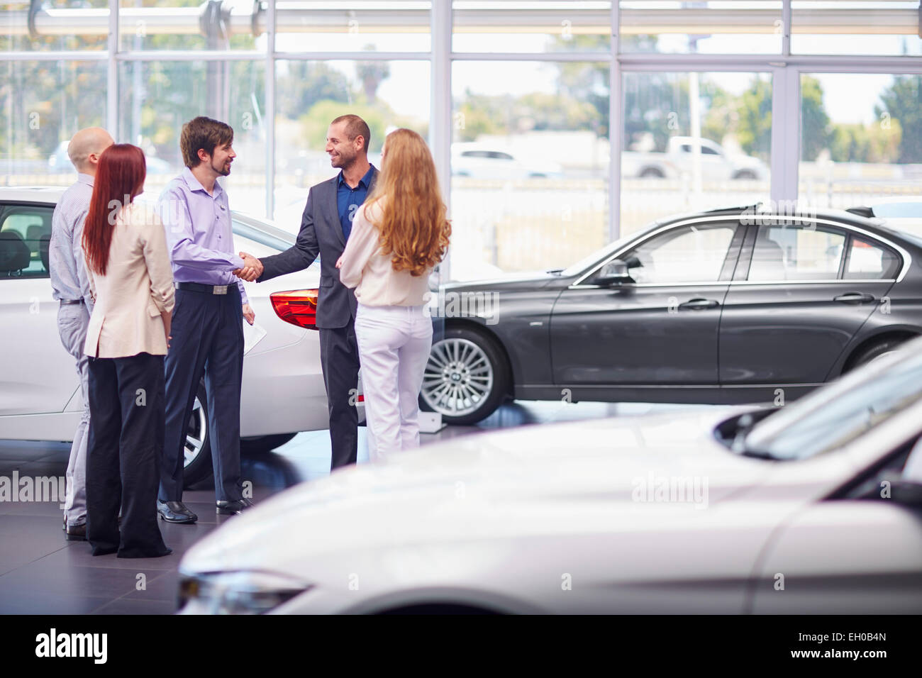 Car dealer meeting with clients in showroom Stock Photo - Alamy