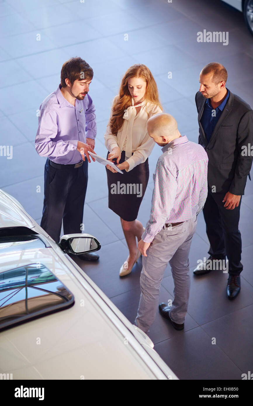 Car dealer meeting with clients in showroom Stock Photo - Alamy