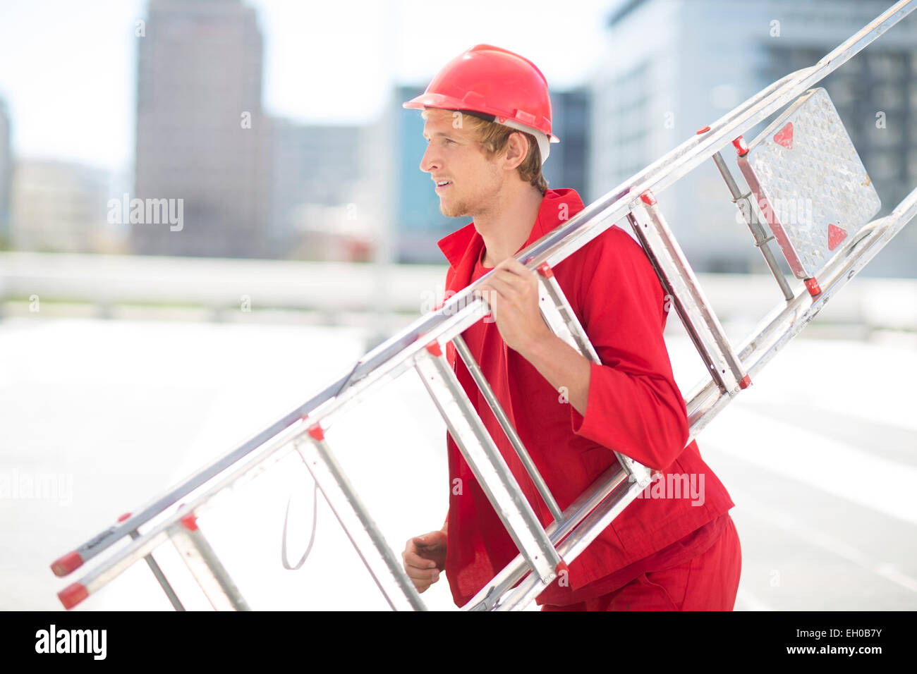 Worker with ladder and safety helmet dressed in red Stock Photo - Alamy