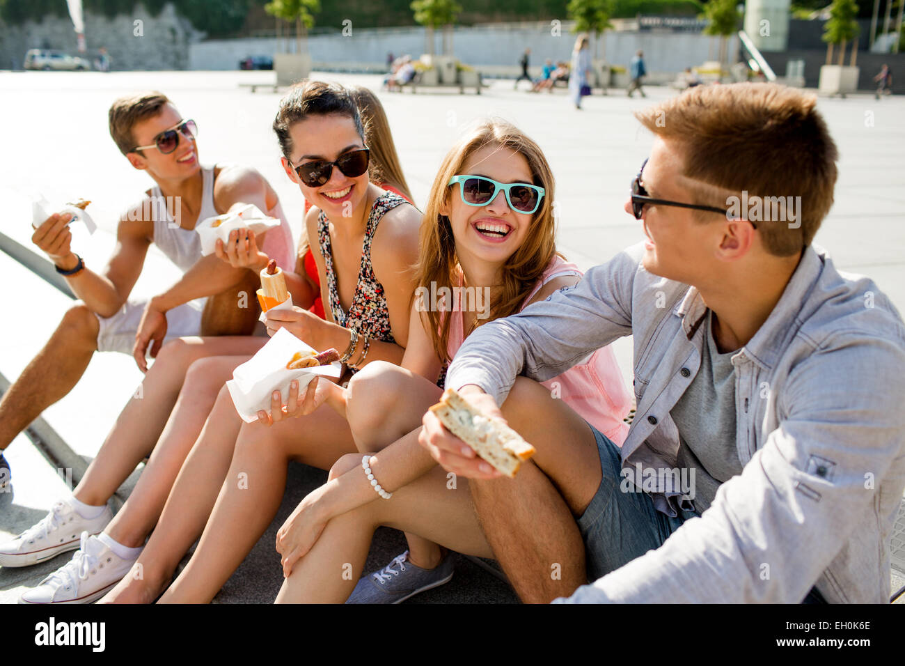 group of smiling friends sitting on city square Stock Photo - Alamy