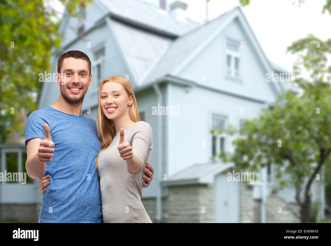 smiling couple showing thumbs up over house Stock Photo - Alamy