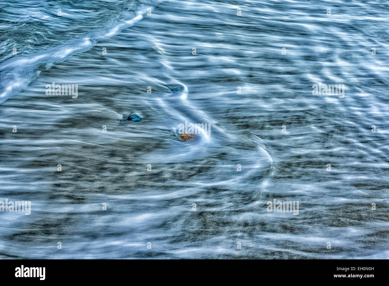 Waves washing over small rocks on a beach. Enhanced detail and contrast ...